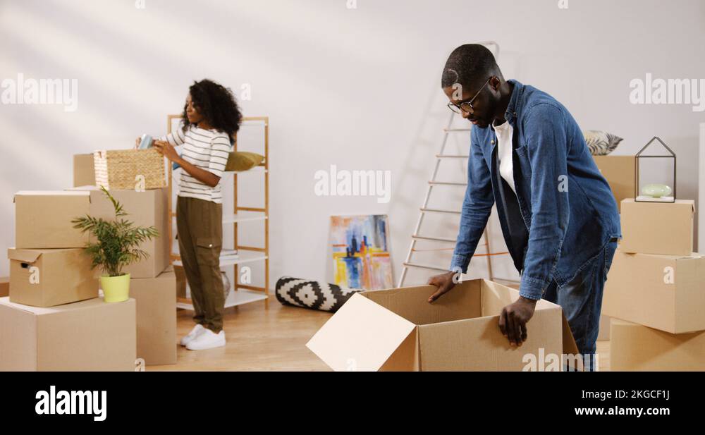 Handsome young African American man unpacking the carton box and his ...