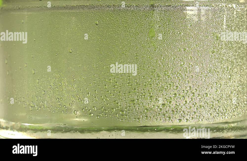 Drops of pure water or alcohol drip inside a glass jar, on green back ...