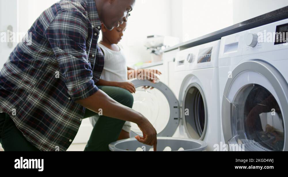 Side view of black father and son washing clothes in washing machine at ...