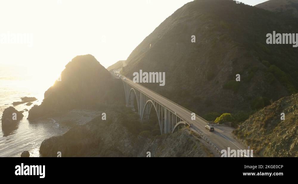 Cars crossing bridge spanning mountains on coastal highway - aerial ...