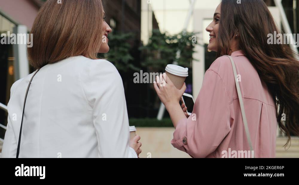 Back view on the two young girls best friends drinking coffee, walking ...