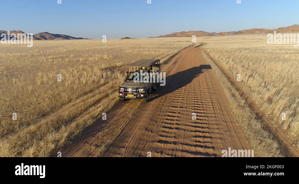 4K aerial zoom out view of a 4x4 safari vehicle driving on a sand track ...