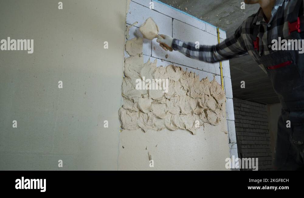 builder in work wear putting plaster on aerated concrete block wall ...
