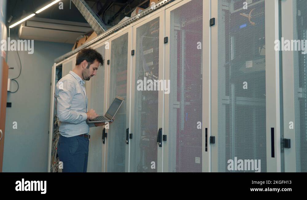 Man Working On Laptop In Server Room Checking Rack Server Cabinet And ...