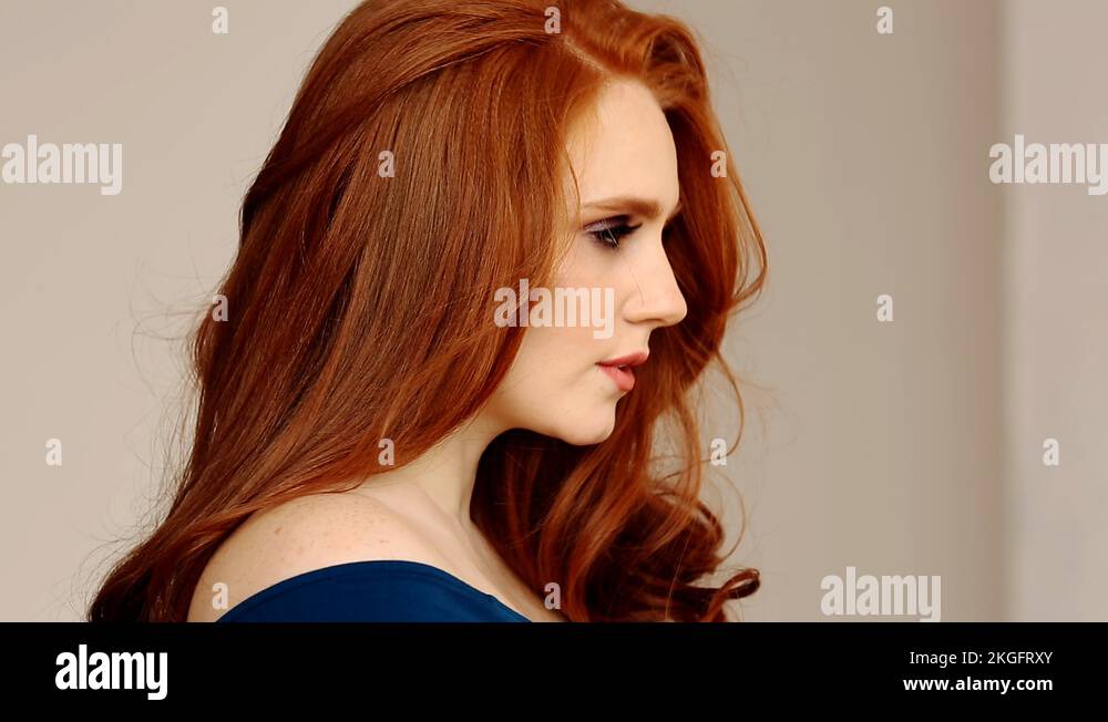 SIDE VIEW: Portrait of red head woman in blue dress poses and smiles in ...