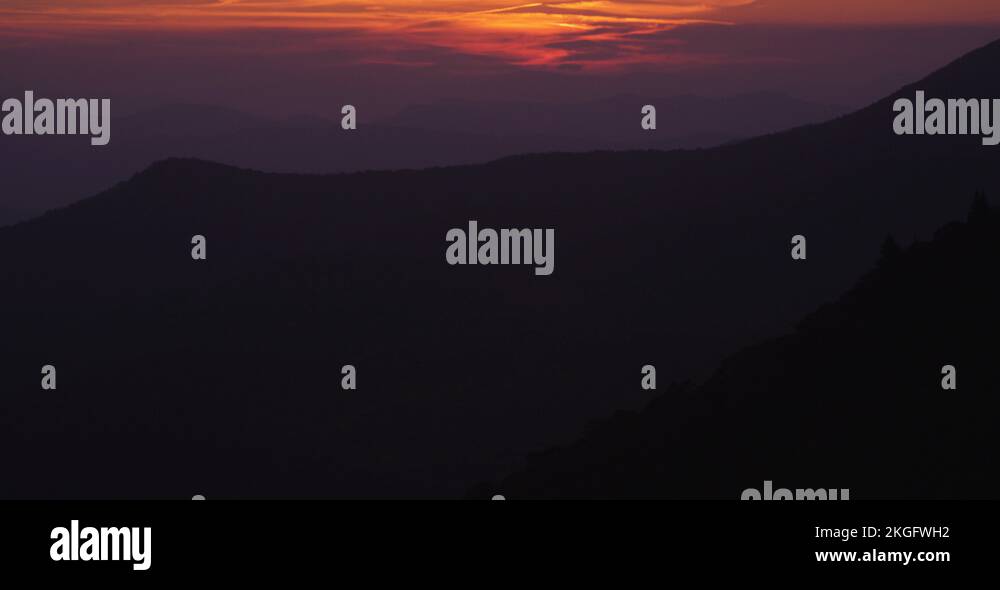 Vapor trails in the orange sunset sky and silhouetted mountain ranges ...