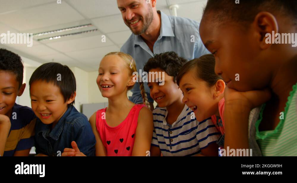 Adult Caucasian male teacher teaching kids on laptop in classroom at ...
