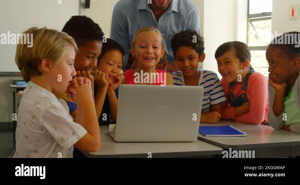 Adult Caucasian male teacher teaching kids on laptop in classroom at ...