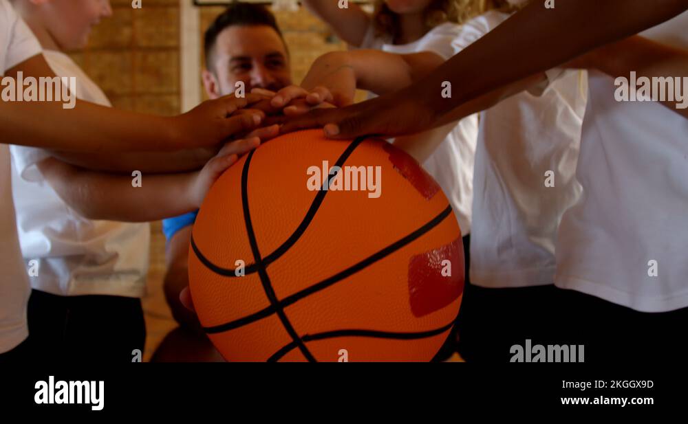 Basketball coach and schoolkids forming hand stack in the basketball ...
