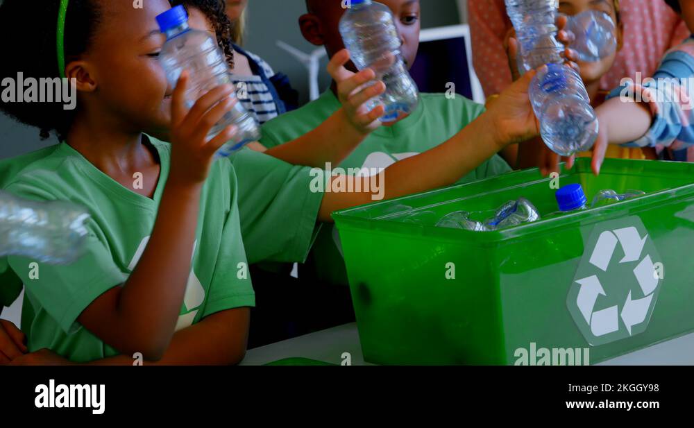 Schoolkids putting bottles in recycle container at desk in classroom 4k ...
