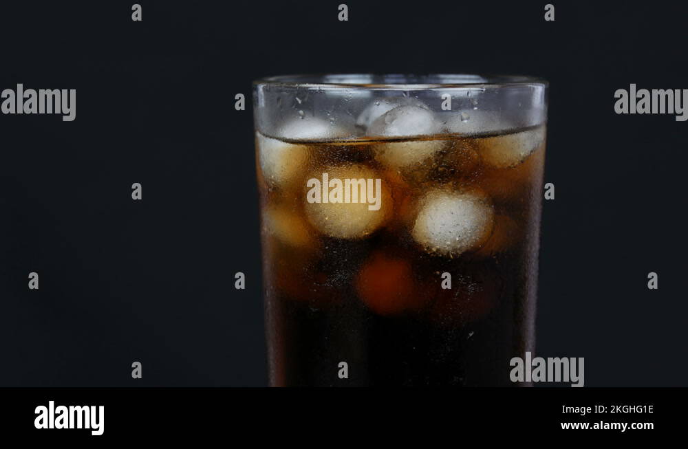 Bubbles of cold cola in a transparent long glass with ice rotating on a ...