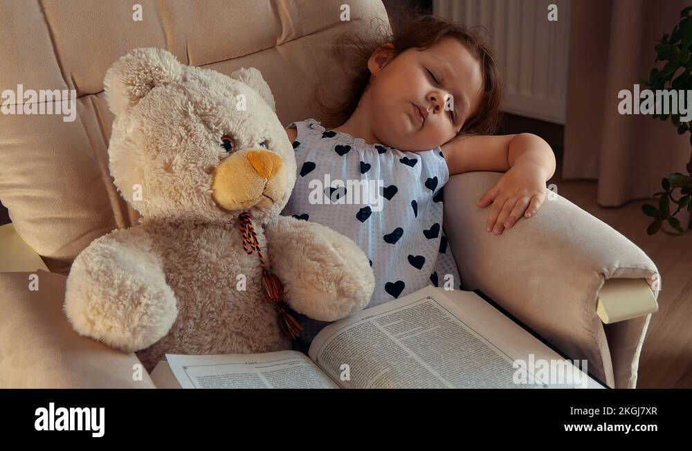 Little girl sleeping on the chair with big book hugging toy teddy bear ...