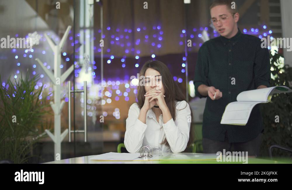 Angry boss walks around the table at which the junior manager is ...