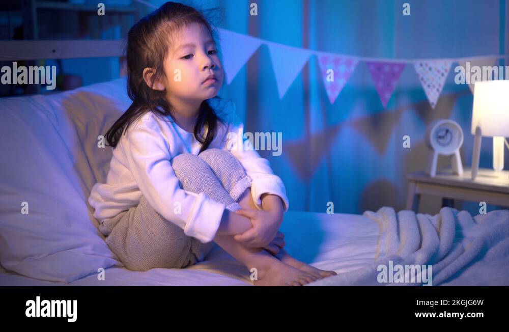 Sad child girl hug her knee and crying on the bed in a dark bedroom at ...