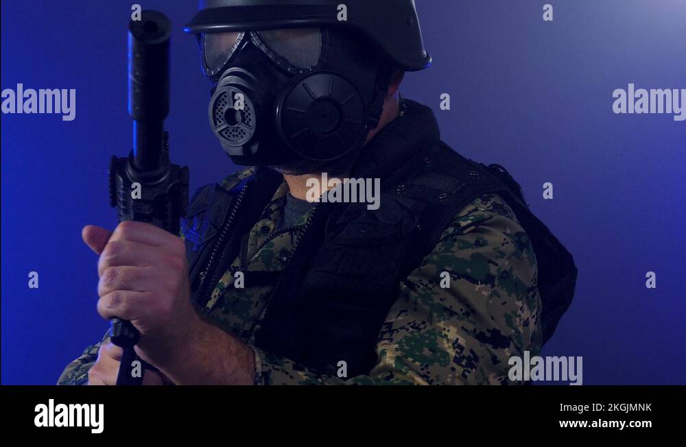 Soldier in gas mask turns around and points assault rifle in blue smoke ...