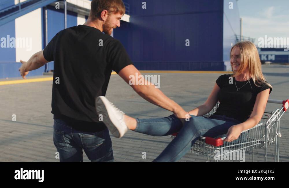 Guy rolls attractive young woman in the trolley on parking lot of ...