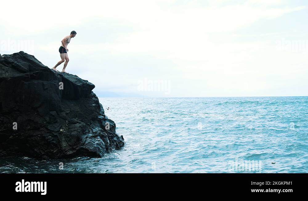 A young man jumping from a cliff into the blue sea. Active and fun ...
