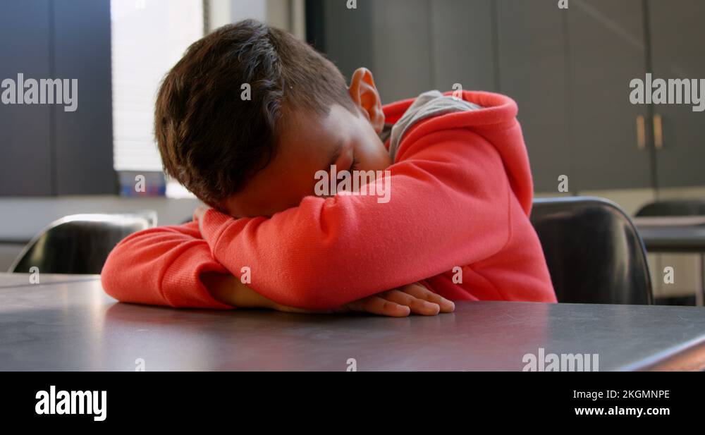 Front view of Asian schoolboy sleeping over the desk in classroom at ...
