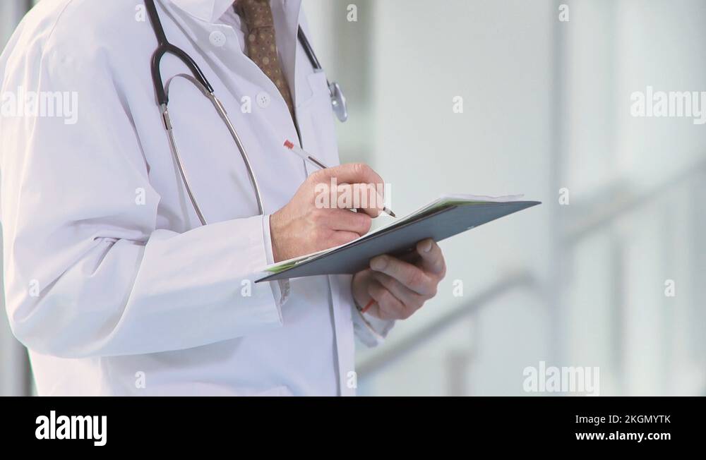 Close-up tilt up shot of a doctor in a lab coat writing on a chart and ...
