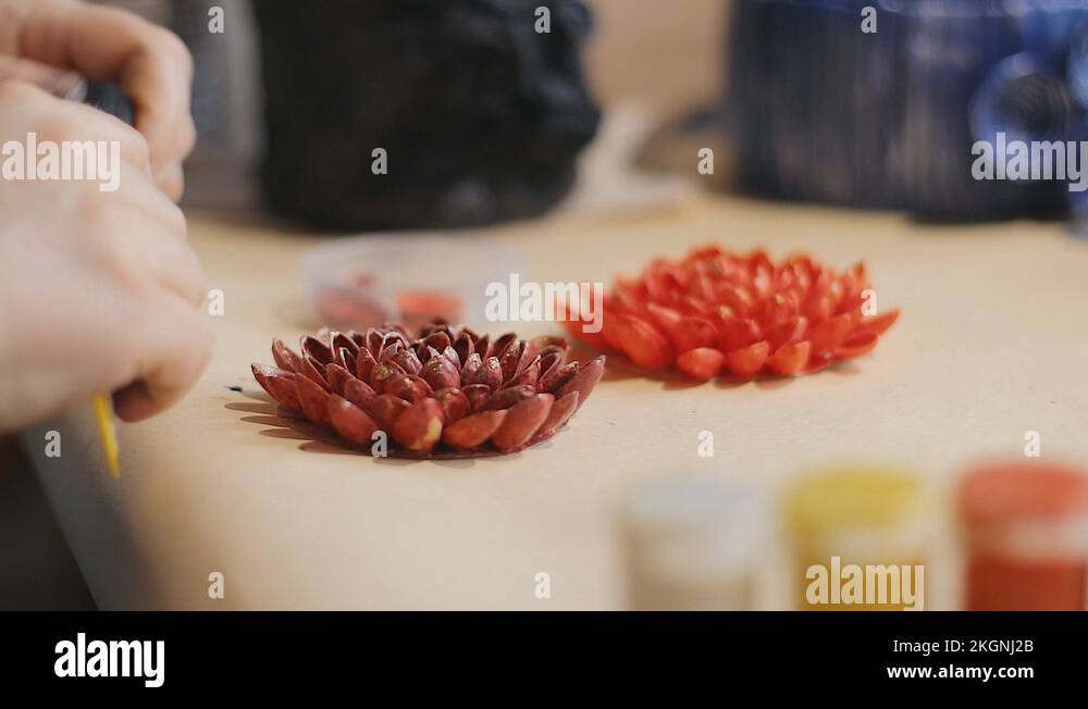 Female artist is making a design of decorative flowers with painted nut ...