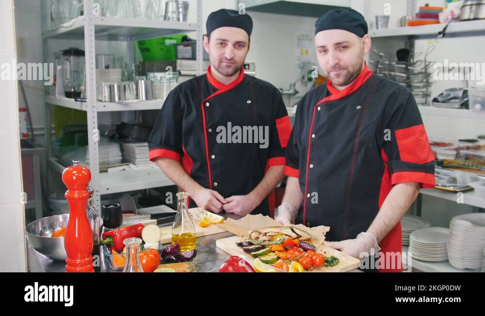 Restaurant kitchen. Two men chefs finished serving the dish, taking it ...