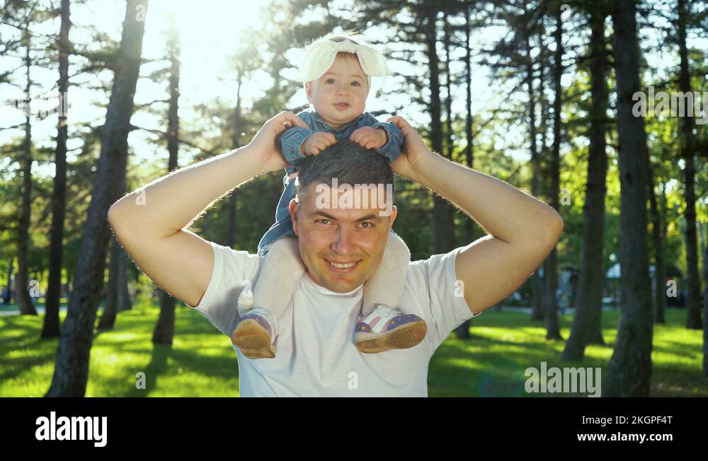 lens flare on smiling father holding his toddler daughter on shoulders outdoors Stock Video ...