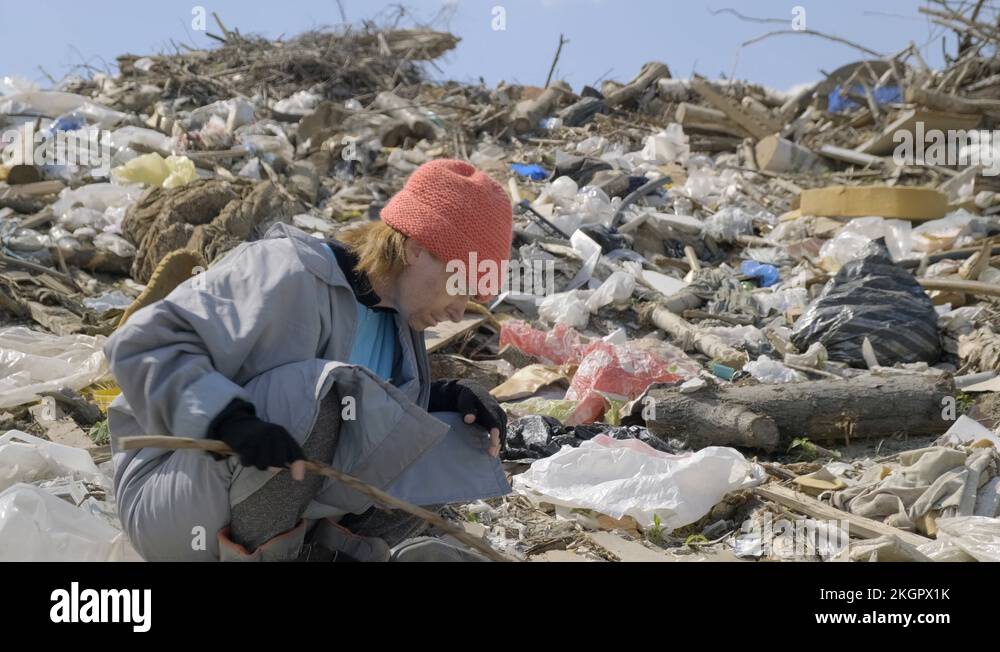 homeless man eats at city dump. bum digs in package of waste in garbage ...
