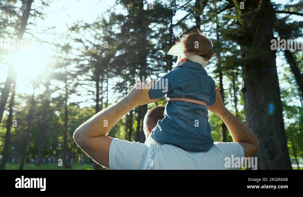 back view of father playing with his baby girl on shoulders in park ...