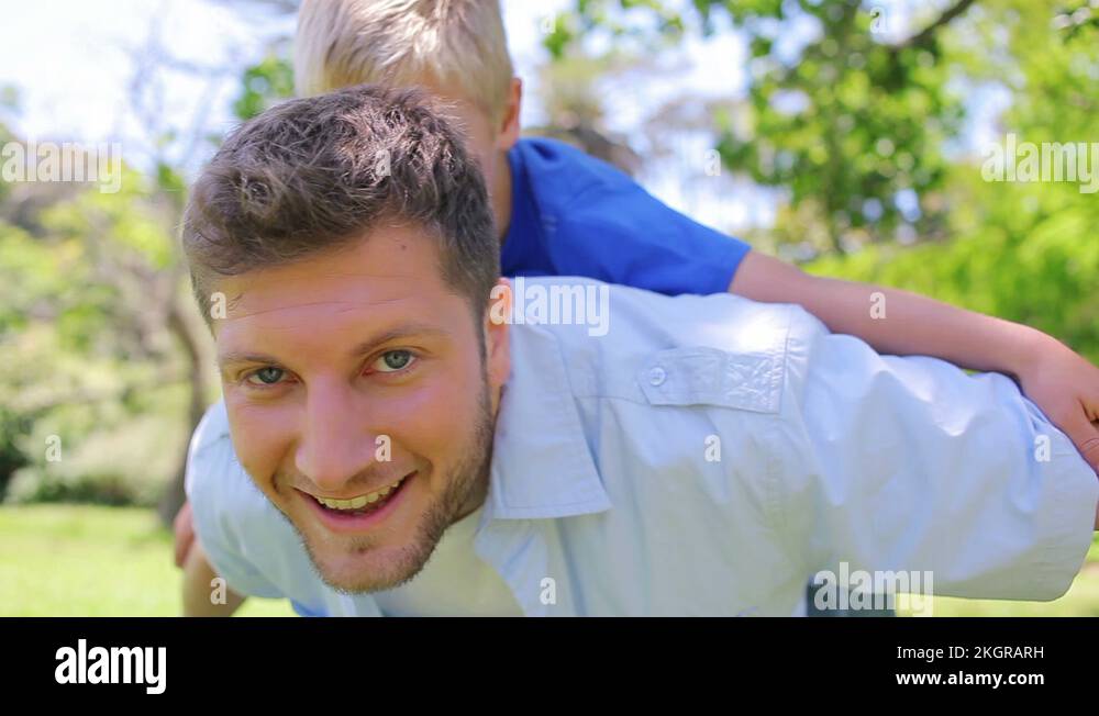 Father giving his son a piggy-back with his arms spread as he smiles ...