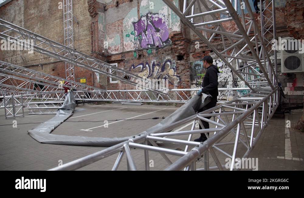 Two young men are mounting grey tarpaulin dome onto metallic stage ...