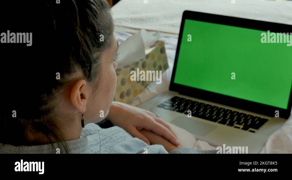 Sick woman talking to a green screen computer while blowing her nose ...
