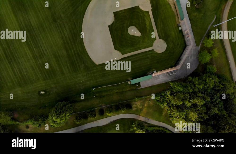 A top down view of a green baseball field in between trees that is ...