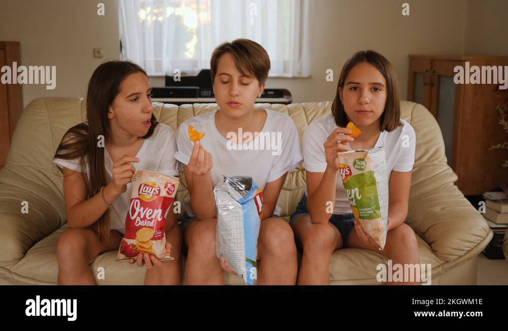 Teenager sisters triplets girls on couch at home eat various potato ...