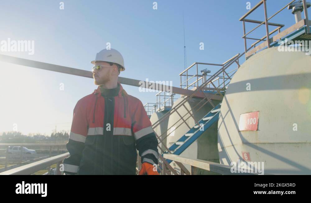 Young petrochemical engineer walks along row of fuel tanks and ...