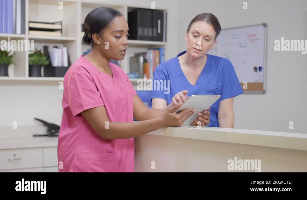 Two nurses at nurses station review patient chart on iPad, camera move ...
