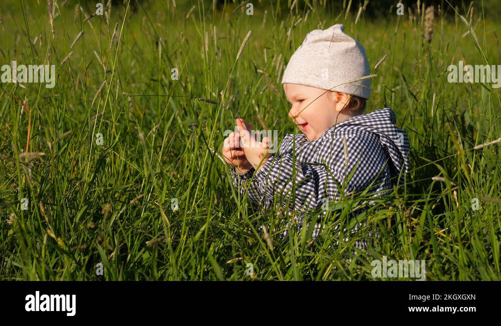 Little baby girl sitting in tall grass, counting on fingers, then look ...
