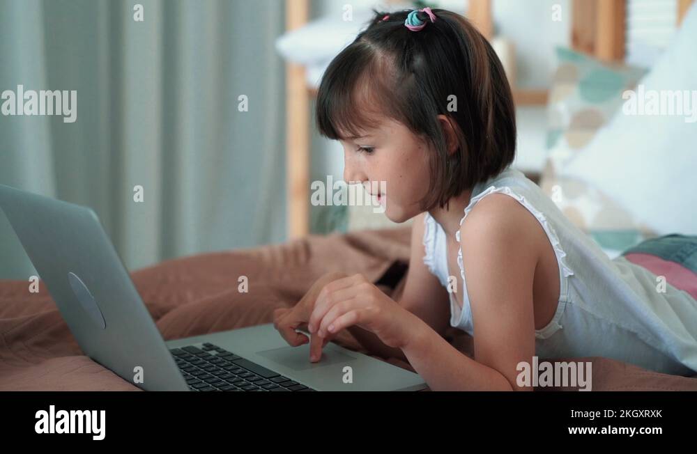 Little girl lying on bed, uses laptop, plays computer game, slow motion ...