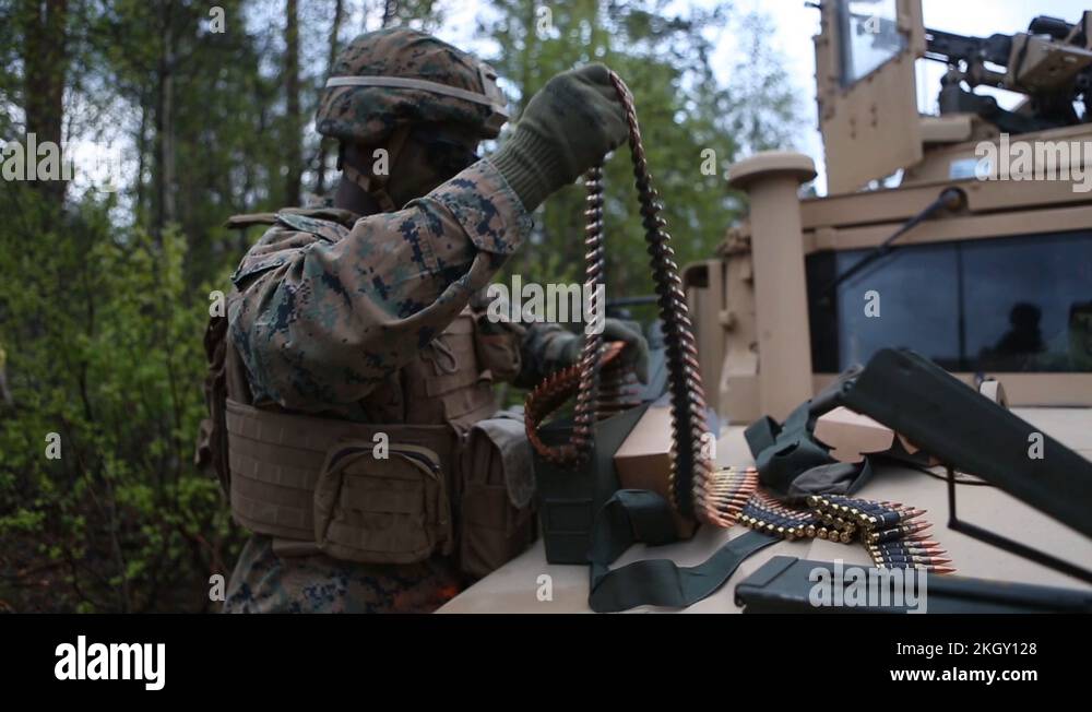 Soldier loading ammunition belt into ammo box on hood of armored ...