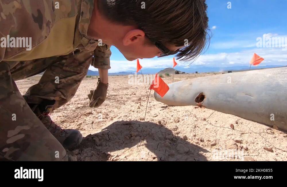 EOD airman inspecting ordnance marked with flags during range clearance ...