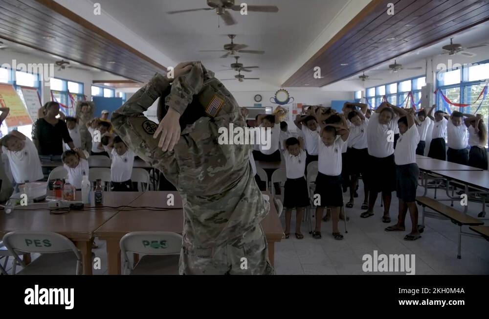 Army medic demonstrating stretching exercises to school children in ...