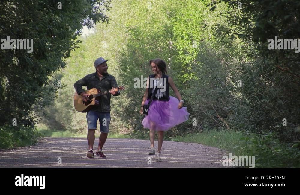 A guy with a guitar and a girl walk merrily along the road. They dance ...