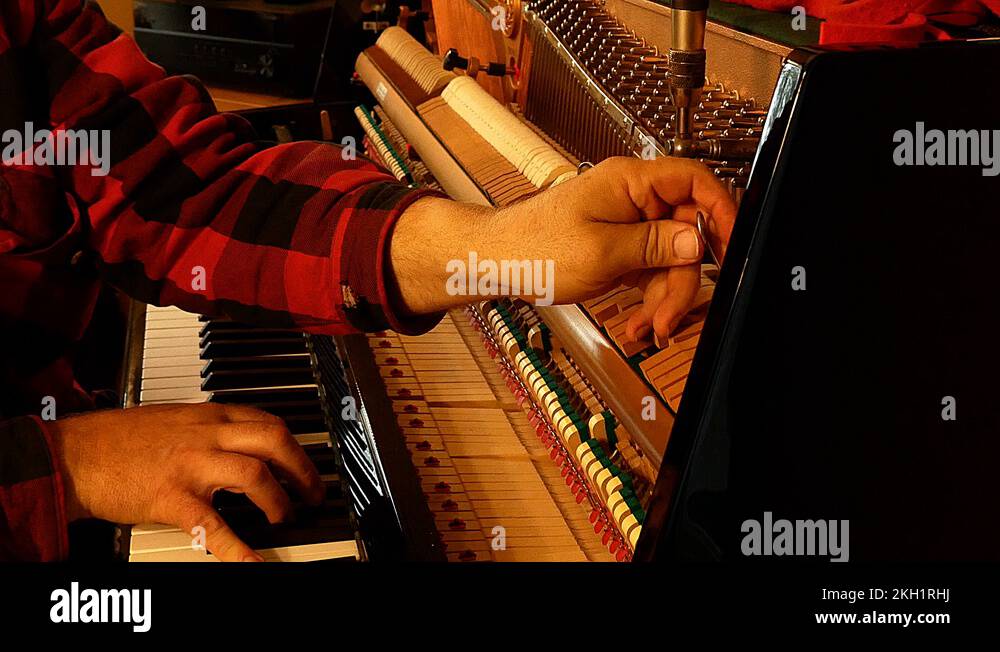 Technician tuning upright piano by playing notes and adjusting pitch of ...