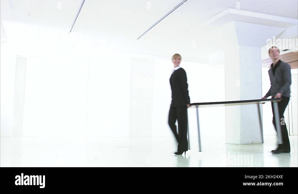 Man and woman carrying a table in a white and empty office premises ...