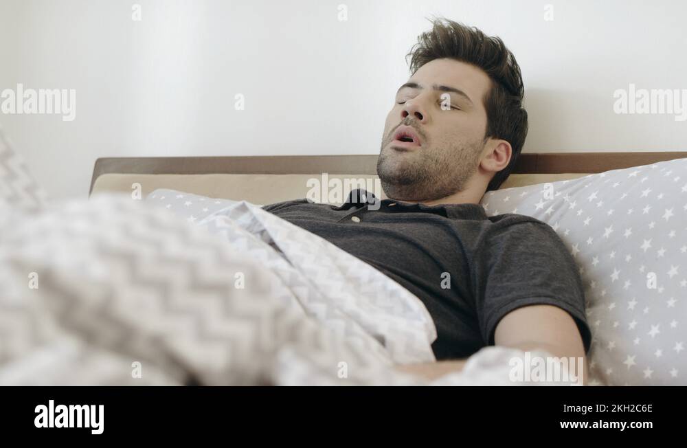 Sleepy man yawning on bed in morning. Handsome guy stretching in ...