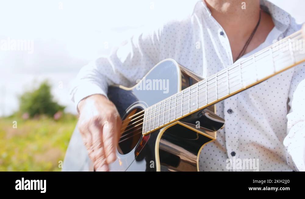 Man plays guitar and sings on nature. Guitarist touching guitar strings ...
