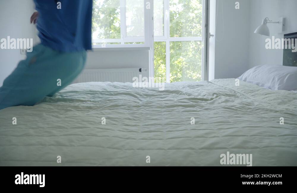 Young tired man falling on the bed holding racket after playing tennis ...