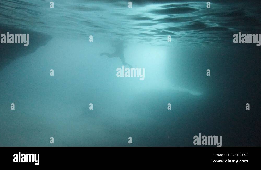 Slow motion underwater swimmer swimming in sea from darkness toward ...