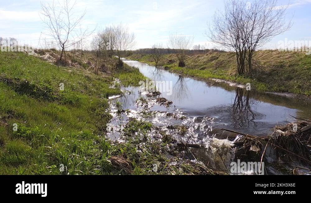 River water flow between green field in spring and garbage dam Stock ...