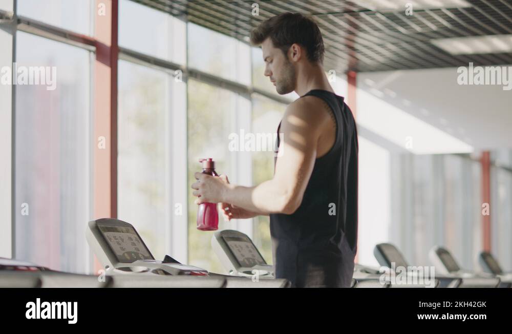 Athlete man drinking water at cardio training on treadmill machine ...