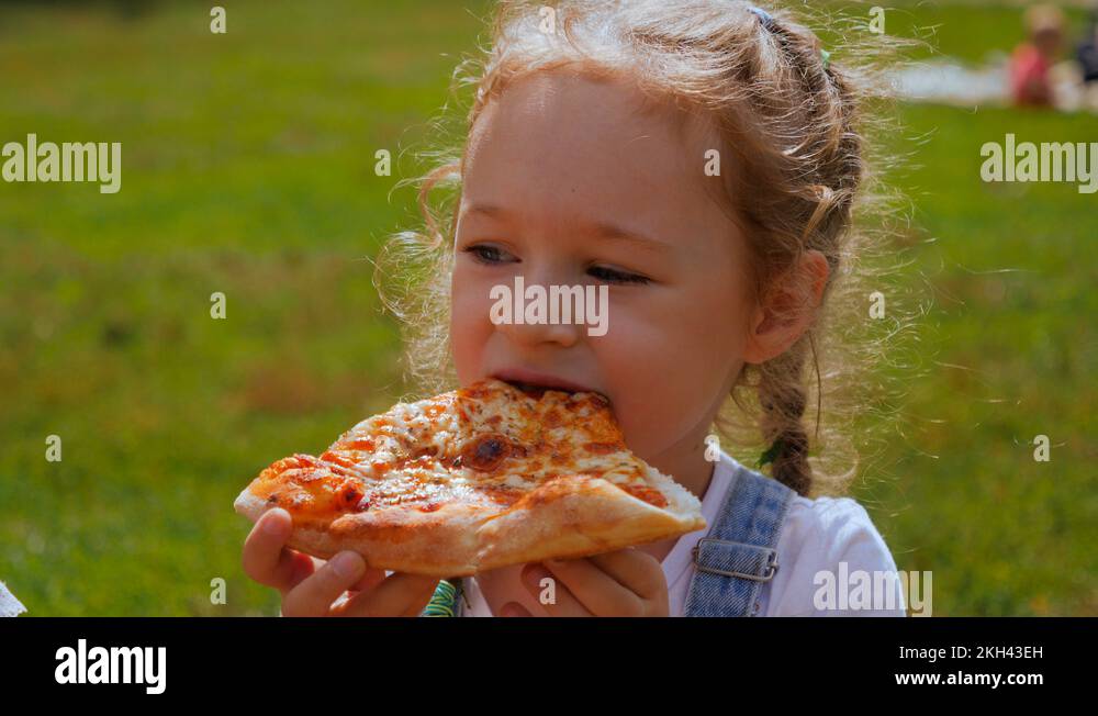 Kid girl portrait picnic eat pizza bite and chew - child with a food on ...